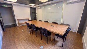 Uma sala de conferência com uma mesa comprida, cadeiras pretas, um quadro branco e uma parede divisória de vidro.