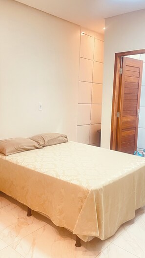 Quarto com cama, almofadas, porta de madeira e parede azulejada.