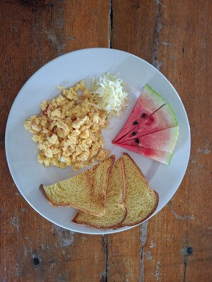 Um prato com ovos mexidos, queijo ralado, fatias de melancia e pão tostado sobre uma mesa de madeira.