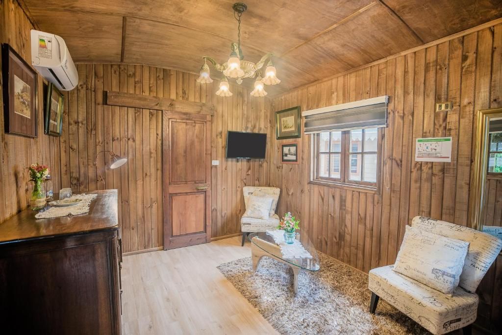 Quarto com painéis de madeira, televisão, escrivaninha, cadeira e sofá.