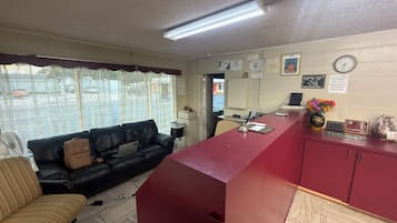 Uma área de recepção de hotel com uma mesa vermelha, um sofá de couro preto e uma janela com cortinas.