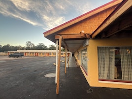 Um motel com galeria coberta, estacionamento e um edifício com placa indicando escritório.