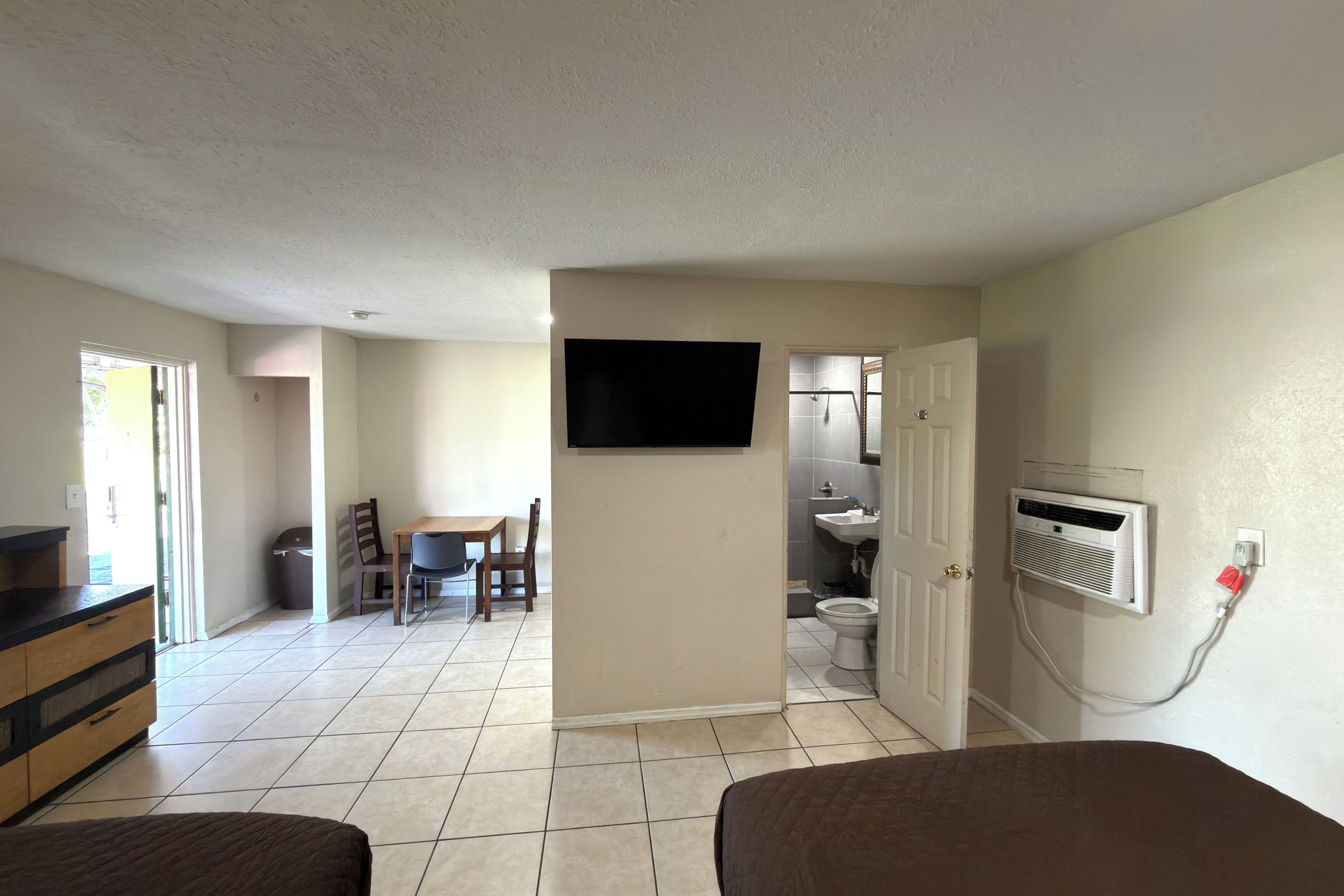 Quarto com cama, escrivaninha, cadeira, televisão e banheiro.