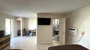 Quarto com cama, escrivaninha, cadeira, televisão e banheiro.