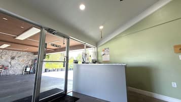 Uma área de recepção com entrada por porta de vidro, balcão de recepção e parede de pedra com um anúncio da Pepsi.