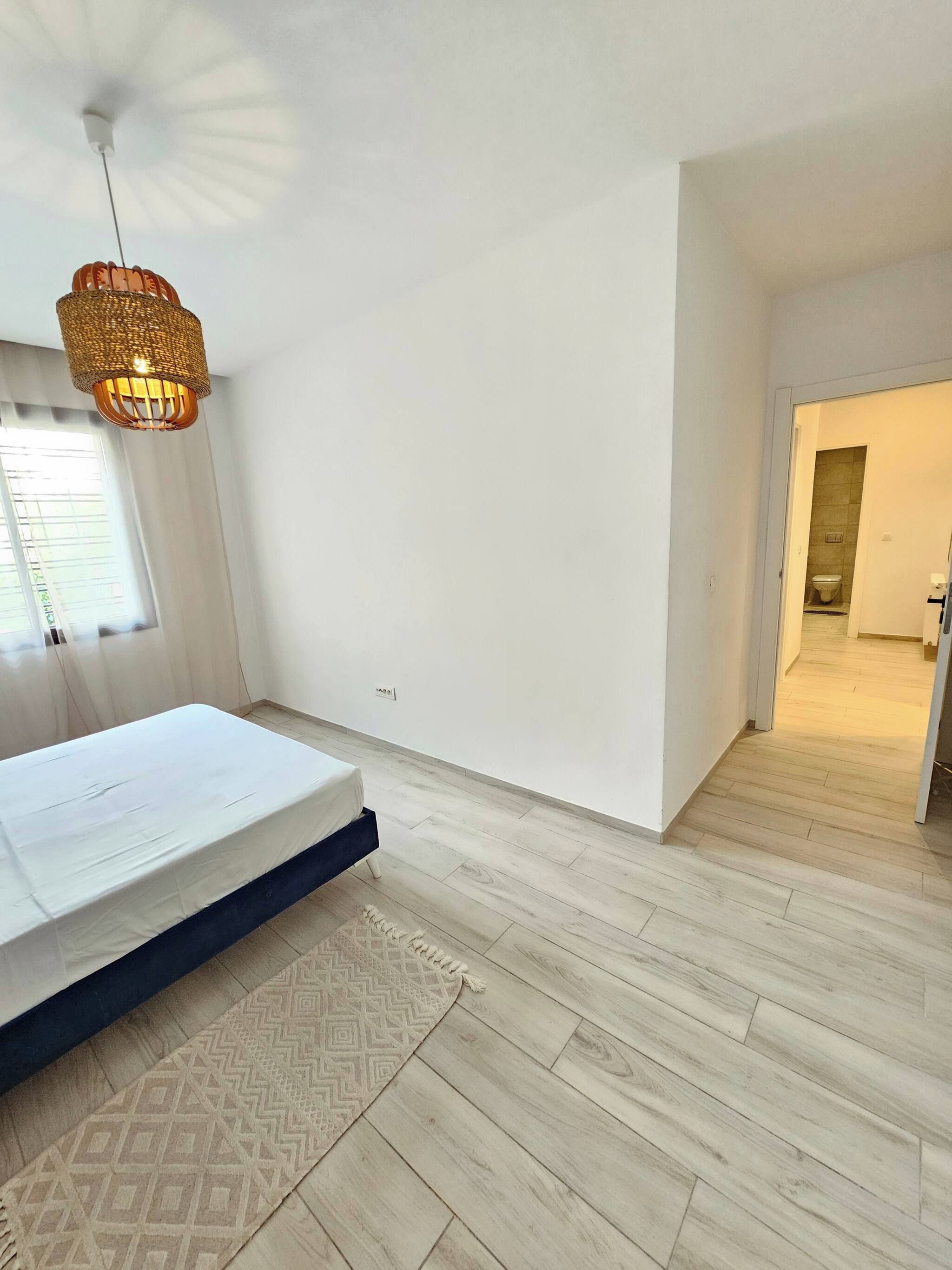 Quarto com cama, luminária pendente e vista para outro cômodo.