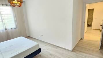 Quarto com cama, luminária pendente e vista para outro cômodo.