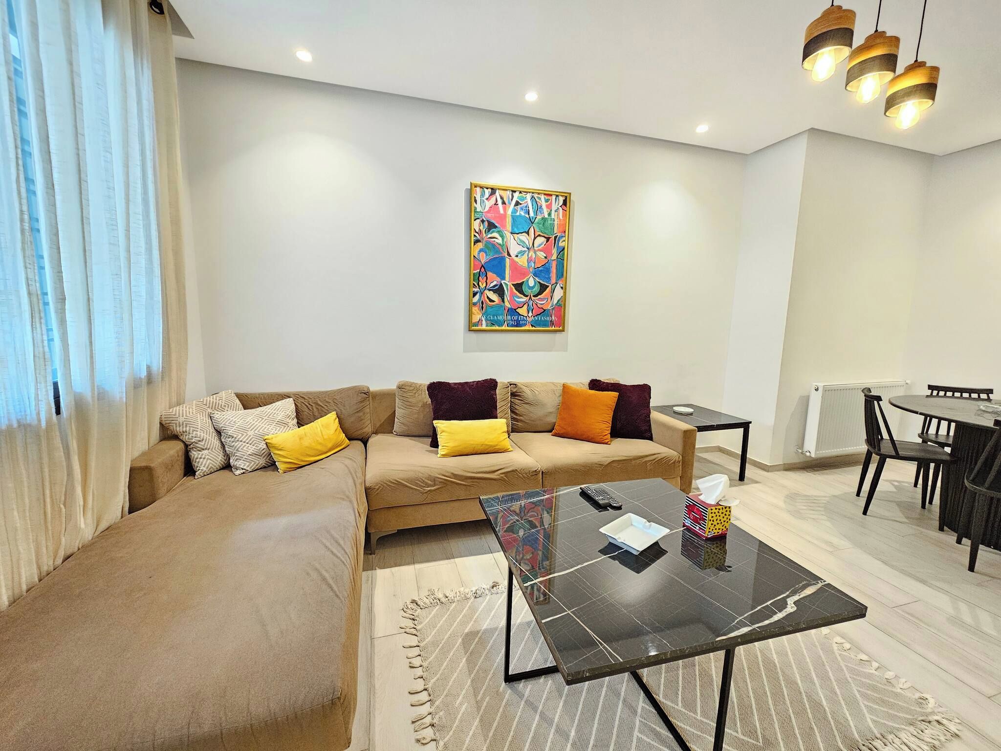 Uma sala de estar moderna com um sofá seccional, uma mesa de centro de vidro e um espaço de jantar com mesa redonda e cadeiras.