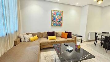 Uma sala de estar moderna com um sofá seccional, uma mesa de centro de vidro e um espaço de jantar com mesa redonda e cadeiras.