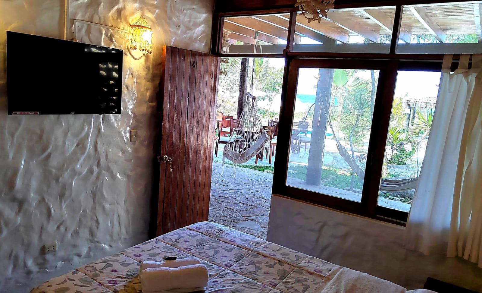 Quarto com cama, televisão na parede e janela com cortinas.