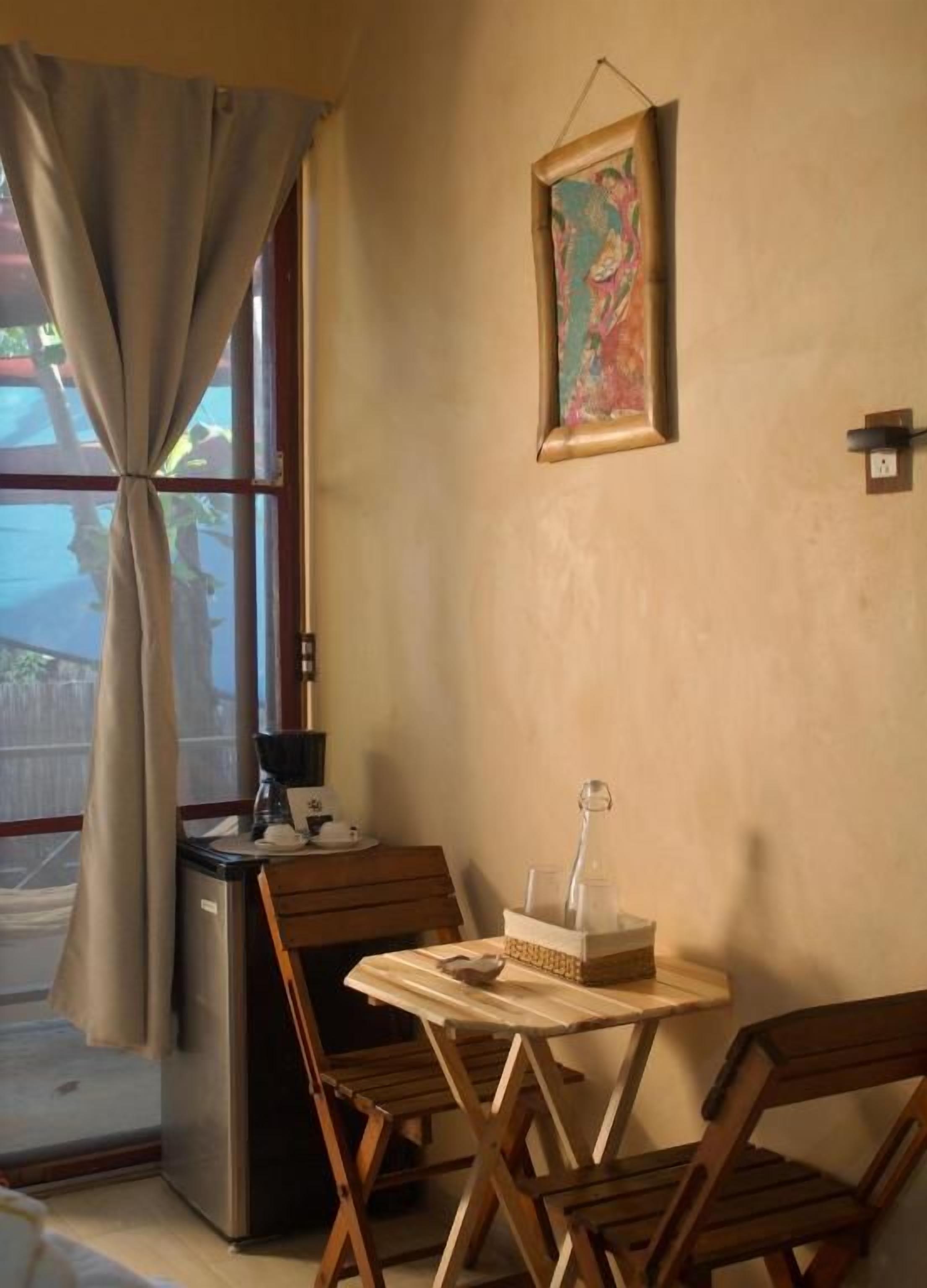 Quarto com mesa de jantar, cadeiras, geladeira, janela com cortinas e um quadro na parede.