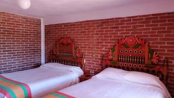 Quarto com duas camas, cada uma com cabeceira de madeira, parede de tijolos e luminária redonda no teto.