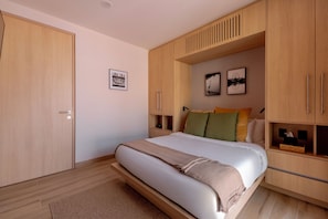 Quarto com cama, guarda-roupa de madeira e uma pequena estante com caixa de lenços.