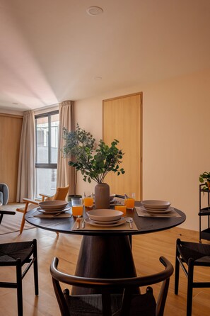 Uma área de refeições com uma mesa redonda, cadeiras, um vaso com plantas e dois copos de suco de laranja.