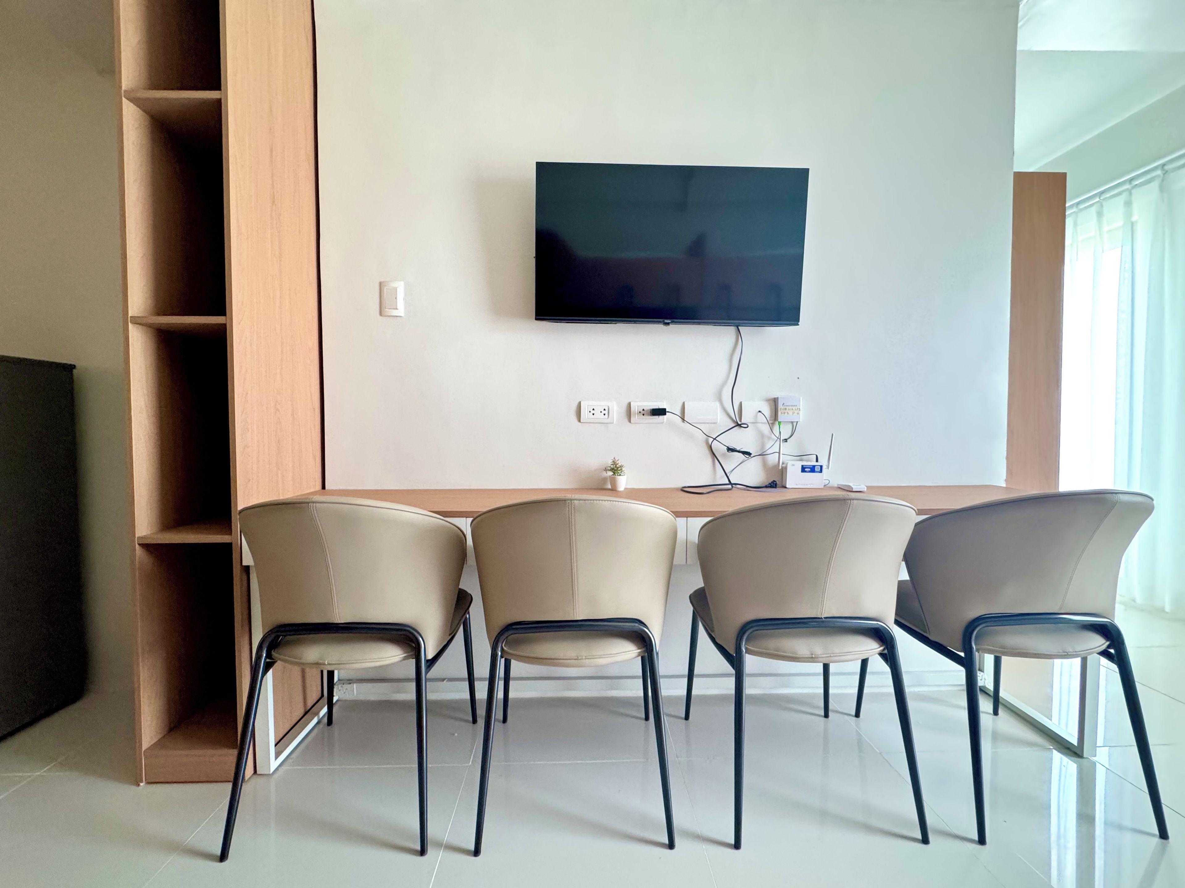 Uma sala de estar moderna com televisão de tela plana fixada na parede, um aparador de madeira e quatro cadeiras bege com estrutura de metal preto.