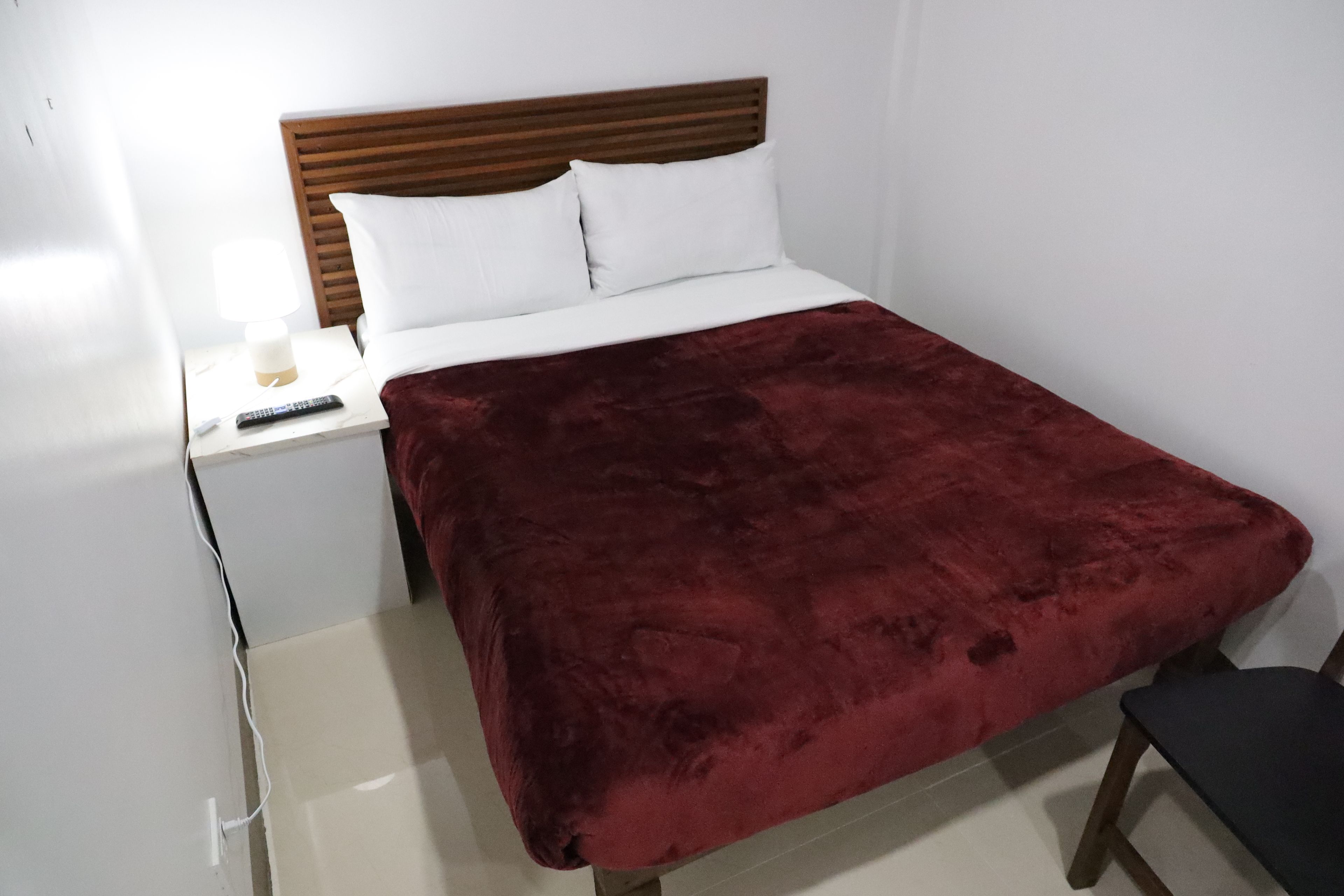 Cama de casal com cabeceira de madeira, roupa de cama branca e manta vermelha.