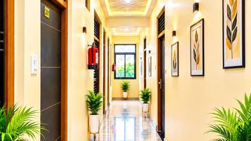Corredor de hotel com piso de mármore, plantas em vasos, quadros e teto decorativo.