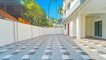 Um pátio com piso de azulejos estampados, parede branca e área coberta com telhado metálico.