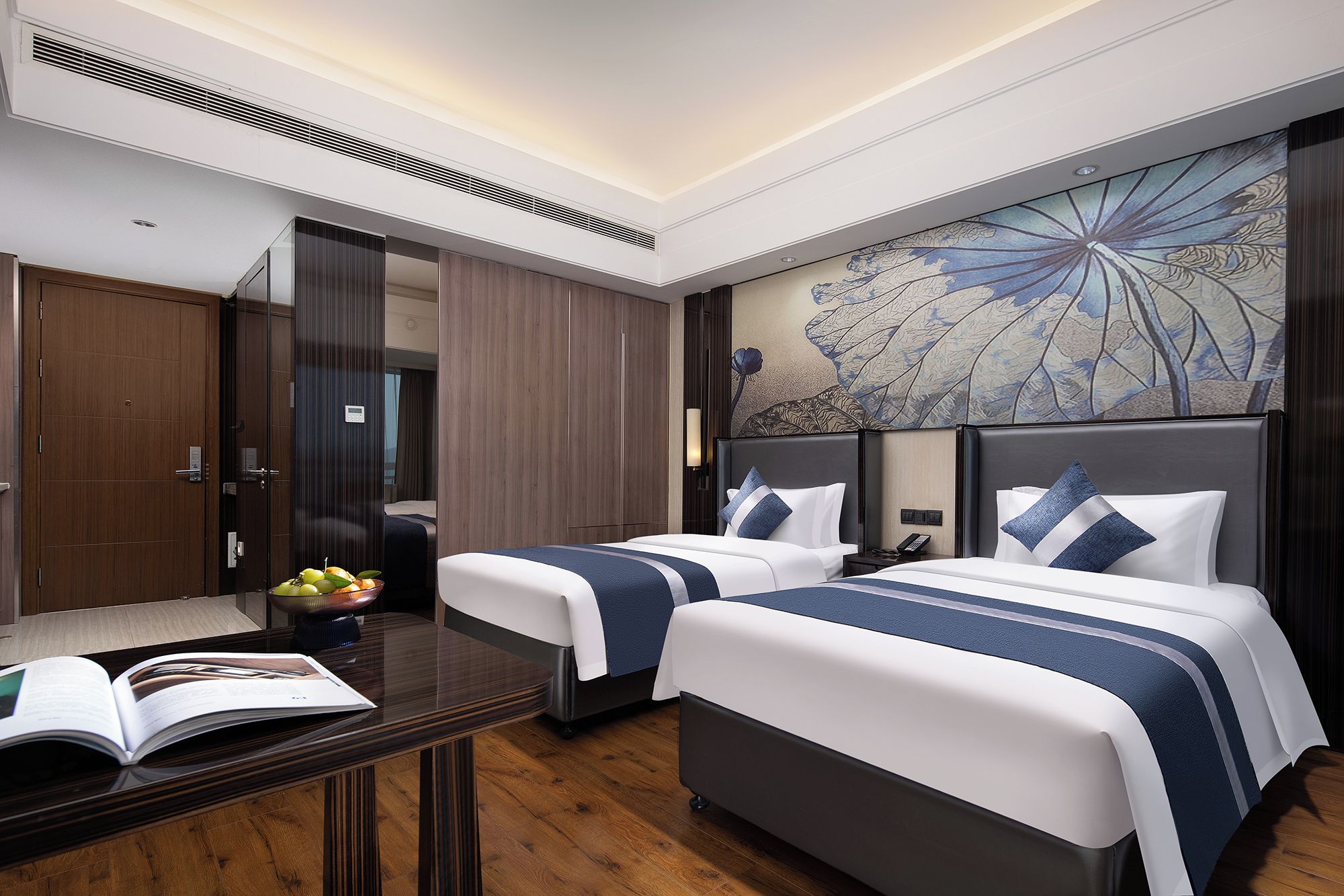 Quarto de hotel com duas camas, uma escrivaninha de madeira, um espelho e um mural decorativo na parede.