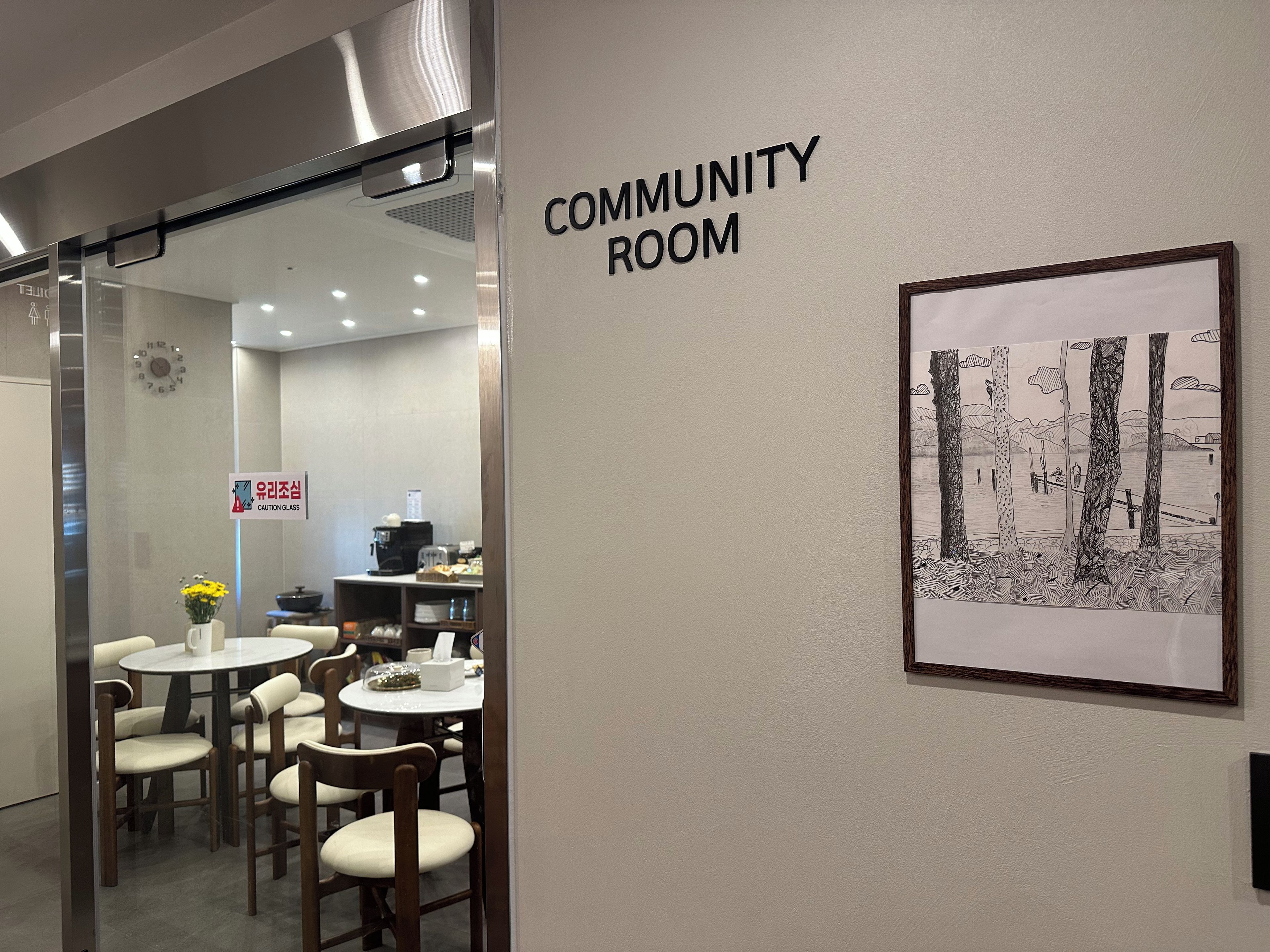 Uma sala comunitária com um relógio, placa de aviso de vidro e um desenho preto e branco emoldurado na parede.