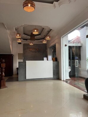 Área de recepção de hotel com balcão, lustres e porta de vidro que dá para o exterior.