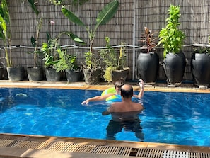 Piscina externa com cerca de bambu e plantas em vasos.