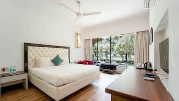 Quarto de hotel com cama, mesa de cabeceira, escrivaninha, cadeira, televisão e ventoinha no teto.