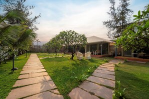 Um jardim bem cuidado com um caminho pavimentado, uma área de estar coberta e diversas árvores e arbustos.