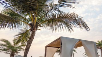 Cenário de praia com cama de dossel, palmeiras e céu claro.
