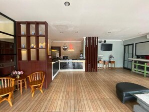Um saguão de hotel com balcão de recepção, piso de madeira e área de estar.
