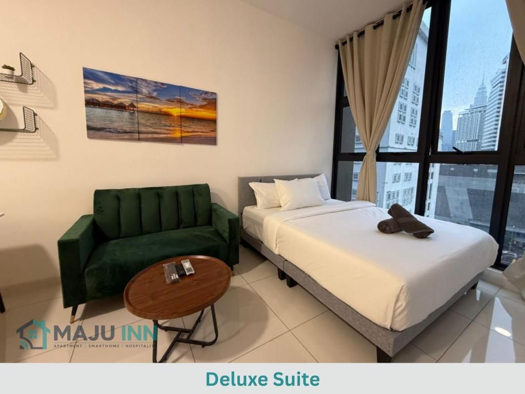 Quarto de hotel com uma cama, um sofá verde, uma mesinha e vista para a cidade.
