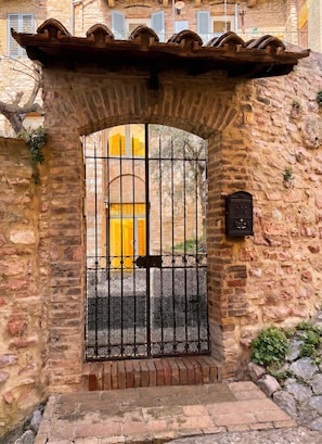 Arco de pedra com portão de metal, caixa de correio e placa numérica.