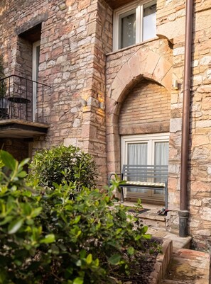 Um edifício de pedra com varanda, um banco e uma janela com cortinas.