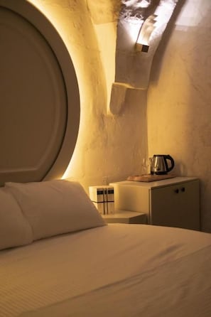 Quarto de hotel com cama, mesa de cabeceira e máquina de café.