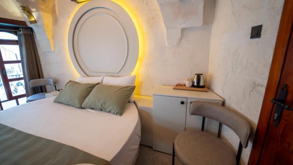 Quarto de hotel com cama, uma pequena escrivaninha, uma cadeira e um detalhe circular na parede.