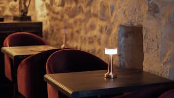 Um quarto com pouca luz, paredes de pedra, uma mesa e cadeiras.