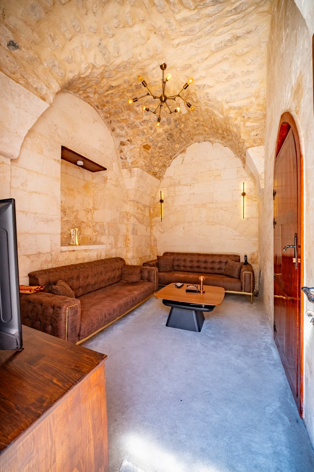Quarto com paredes de pedra, um sofá moderno, uma mesa de centro de madeira e uma televisão.