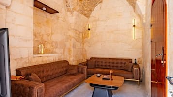 Quarto com paredes de pedra, um sofá moderno, uma mesa de centro de madeira e uma televisão.