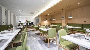 Uma zona de refeições moderna com bancos verdes e mesas, paredes de painel de madeira e iluminação pendente.
