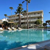 Piscina límpida com espreguiçadeiras e palmeiras, rodeada por um edifício de vários andares.