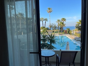 Uma varanda com vista para uma piscina, palmeiras e o oceano.
