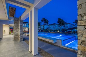 Uma área moderna com piscina ao ar livre, pilares de pedra, vista clara do bairro e piscina bem iluminada.