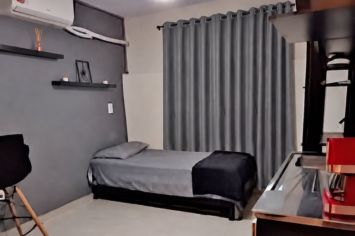 Quarto moderno com cama, escrivaninha, cadeira, ventilador de teto e janela com cortinas.