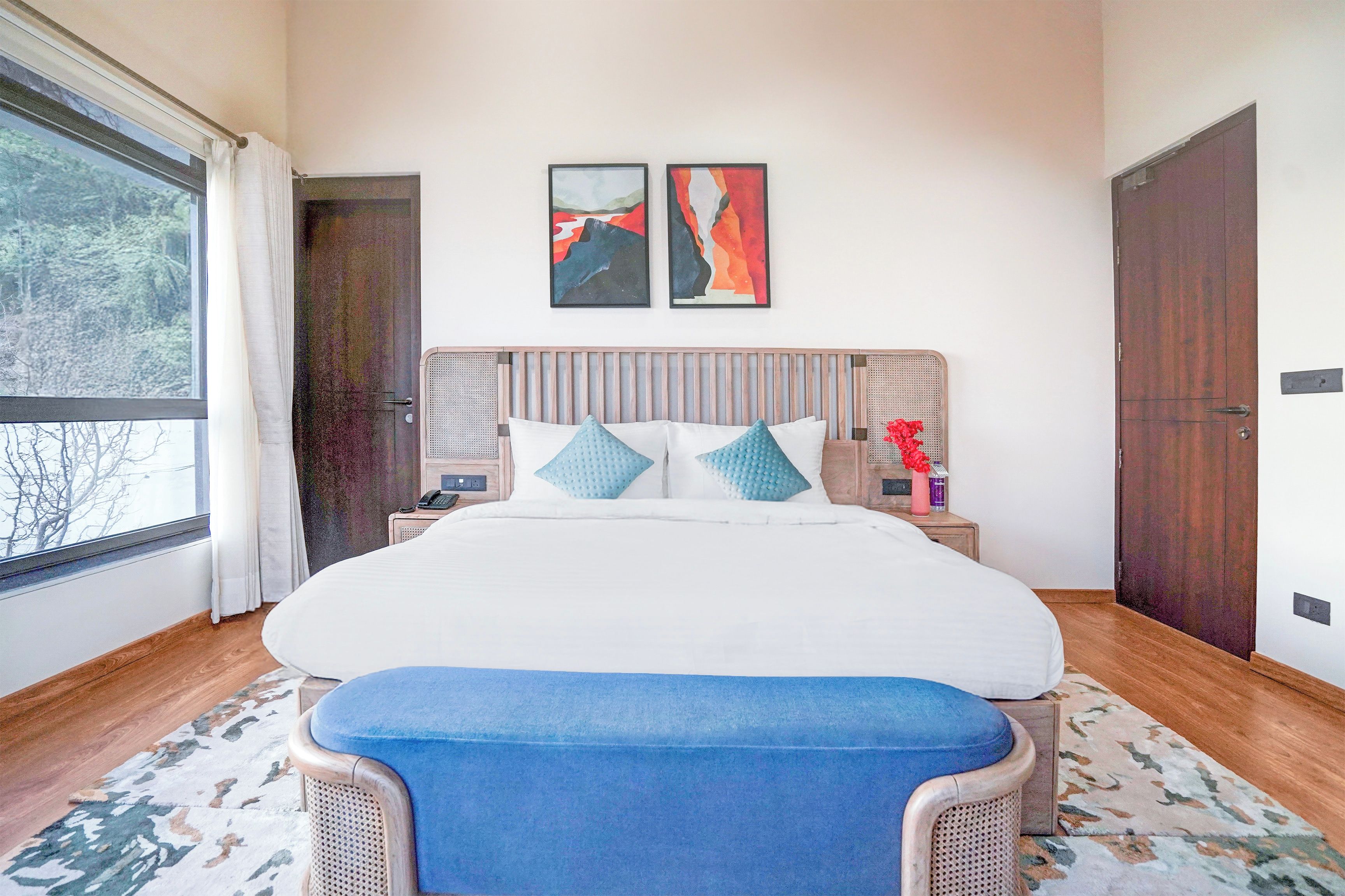 Quarto com cama grande, mesa de cabeceira com abajur e duas pinturas na parede.