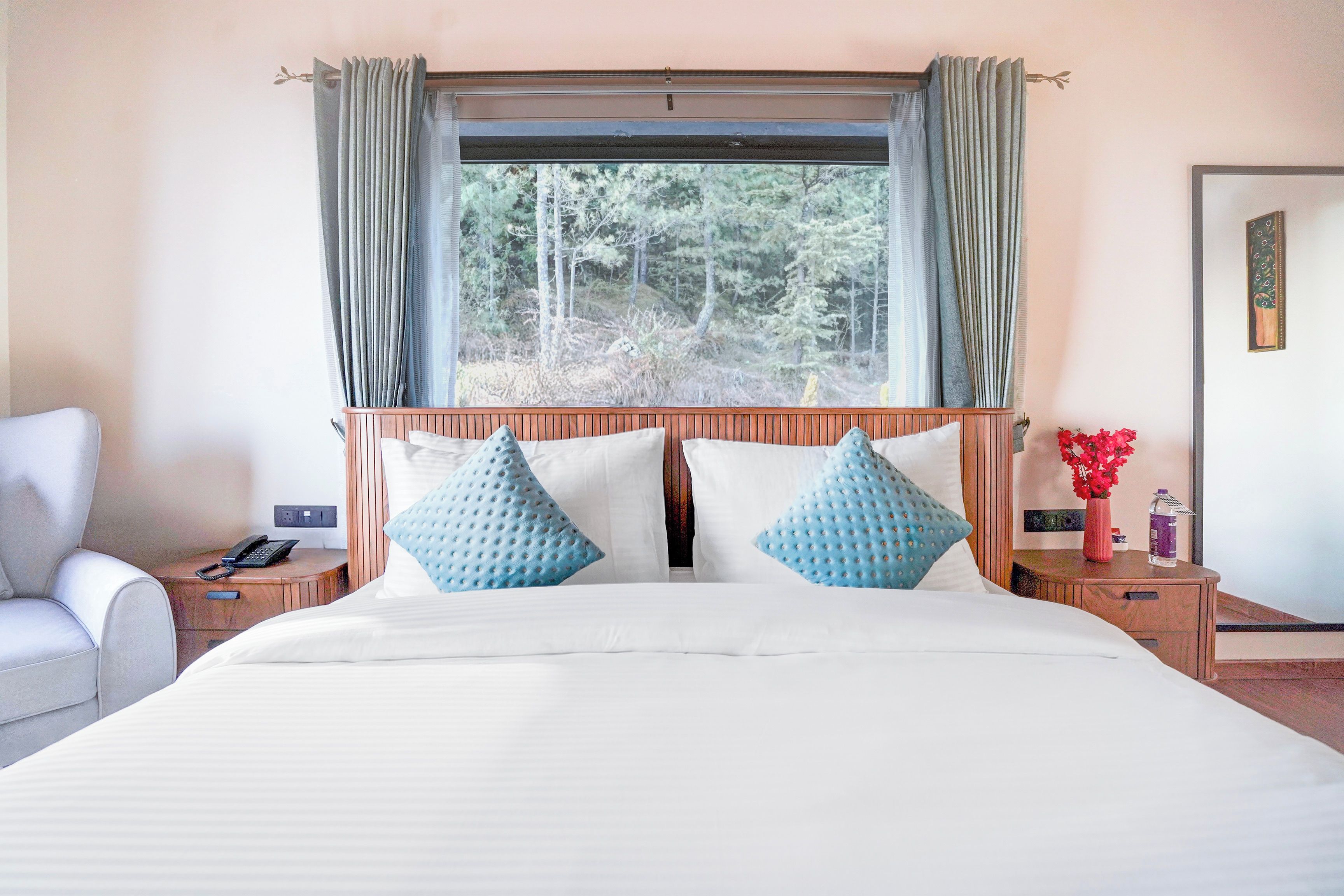 Quarto de hotel com cama grande, duas almofadas, mesa de cabeceira com telefone e janela com cortinas.