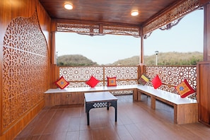 Uma área de estar coberta ao ar livre, com bancos de madeira e uma mesa, cercada por painéis de madeira ornamental.