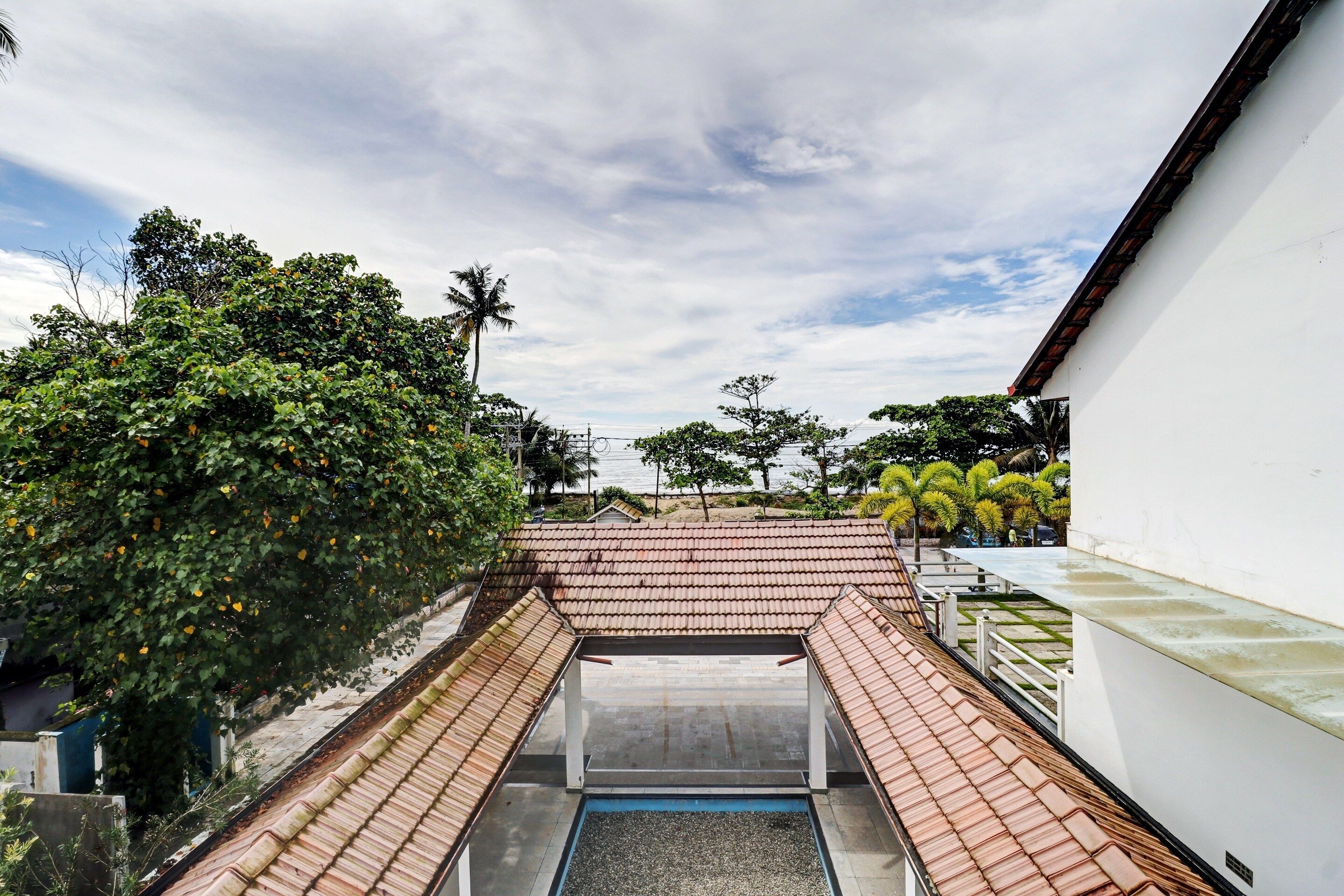 Uma área externa coberta com telhado de metal, cercada por vegetação e um edifício branco.