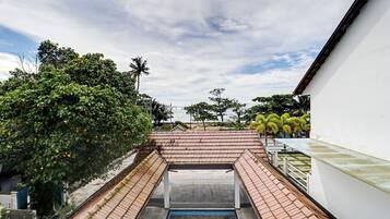 Uma área externa coberta com telhado de metal, cercada por vegetação e um edifício branco.