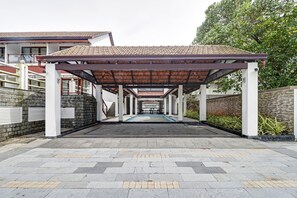 Uma galeria coberta com telhado de azulejos, que leva a um edifício com parede de pedra e portão de metal.