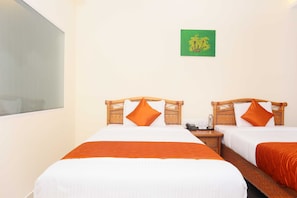 Quarto de hotel com duas camas, cada uma com colcha e almofada laranja, uma pintura de parede verde e uma janela à esquerda.